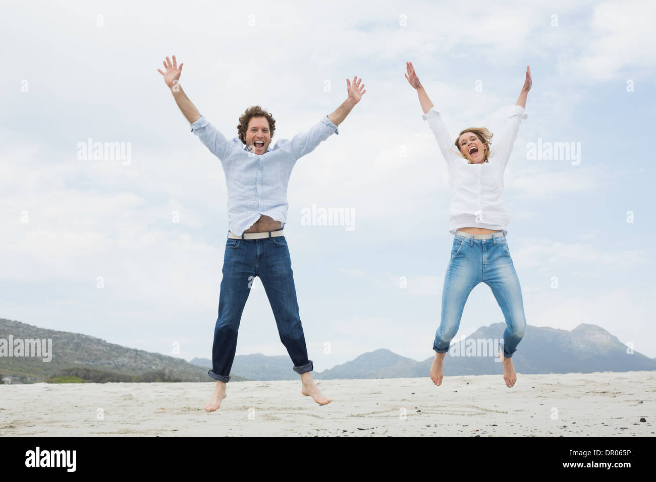 Cheerful young couple jumping at beach Stock Photo - Alamy