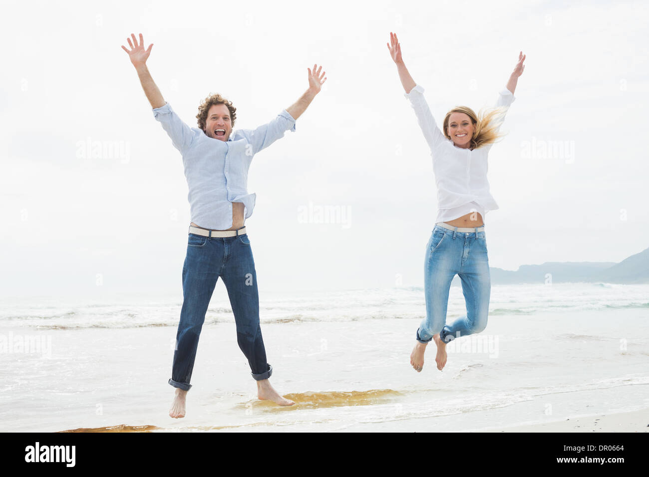 Cheerful young couple jumping at beach Stock Photo - Alamy