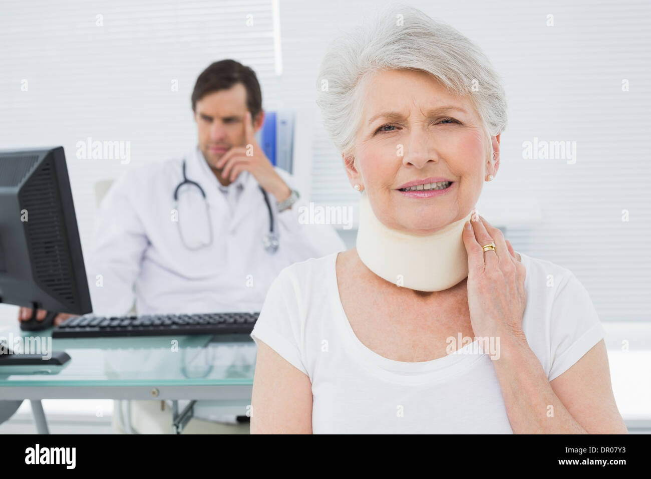 Senior patient in surgical collar with doctor in background at office ...