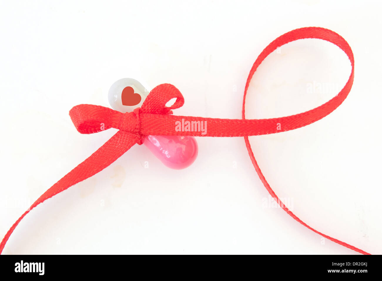Red ribbon tied around a capsule with a heart symbol Stock Photo - Alamy