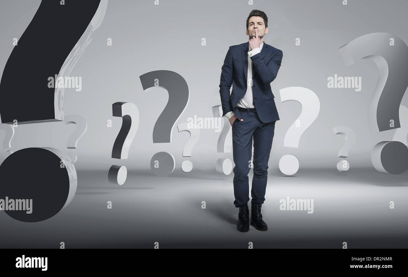 Young smart businessman among question marks Stock Photo - Alamy