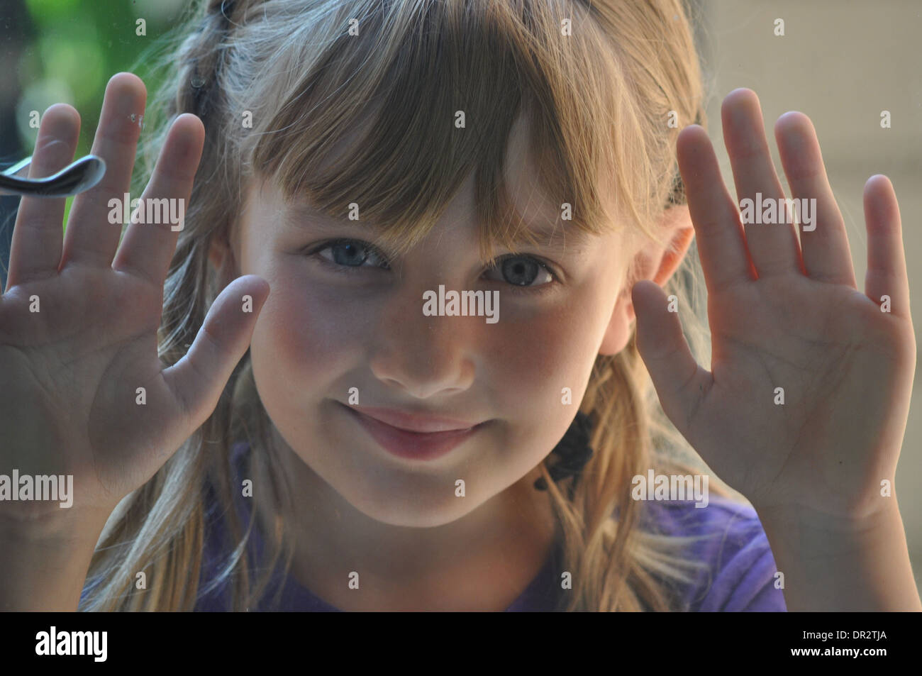 close-up portrait of happy girl pressed against a window looking in ...
