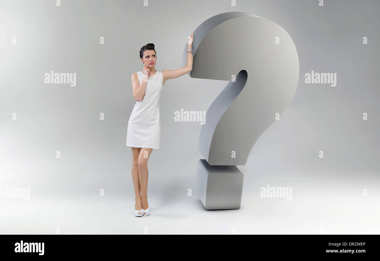 Attractive and astonished woman leaning against the huge question mark ...