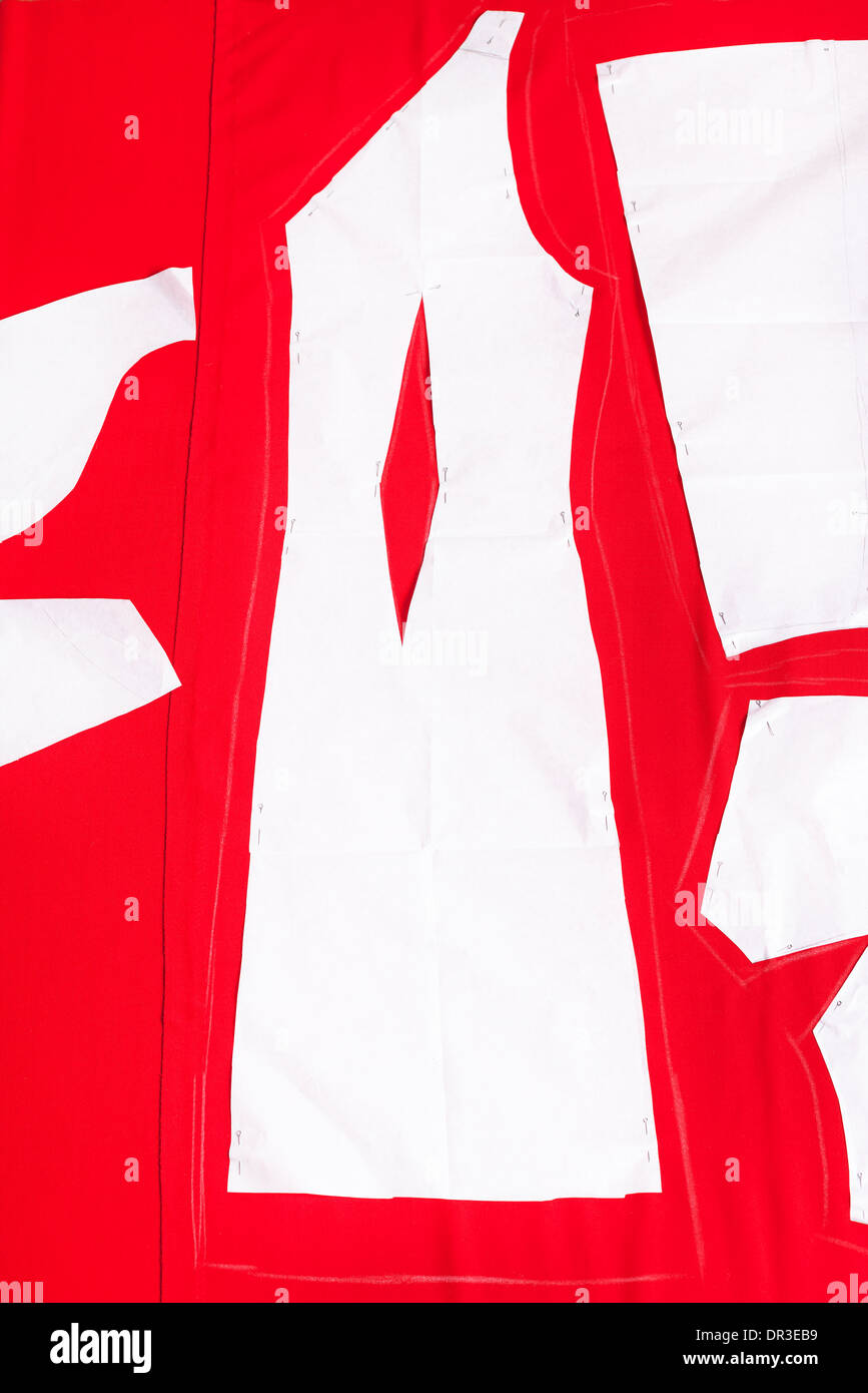 cutting out woolen fabric along pattern lines for tailoring red dress ...