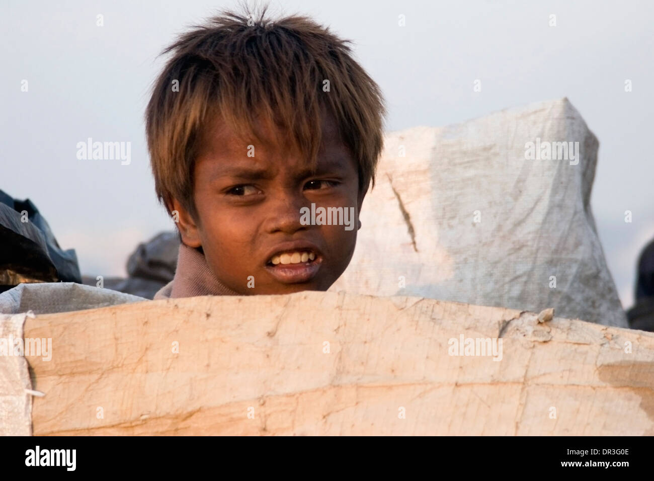 A young child laborer boy is sitting in a big garbage sack at the toxic ...