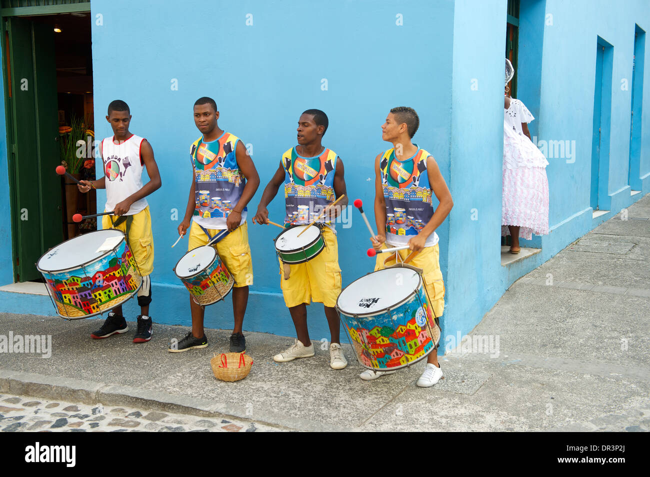 Four young Brazilian men standing on the street drumming against a blue ...