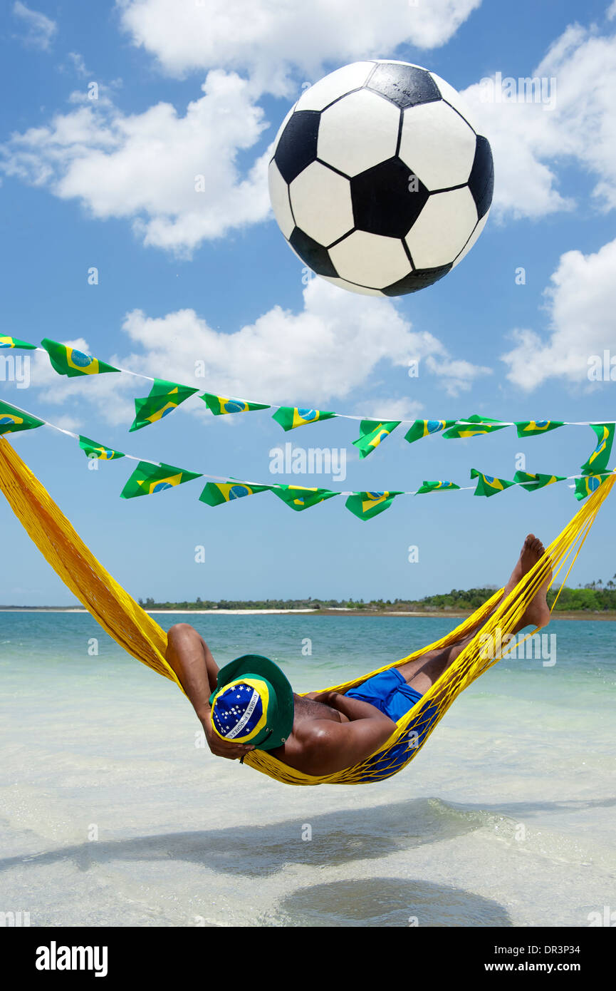 Brazilian soccer fan relaxing in beach hammock with a football floating ...