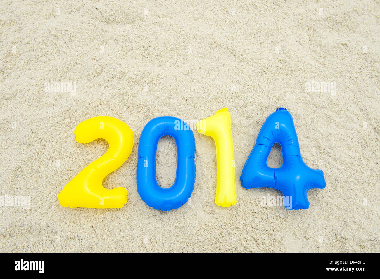 Colorful 2014 message with blue and yellow inflatable numbers on sand ...