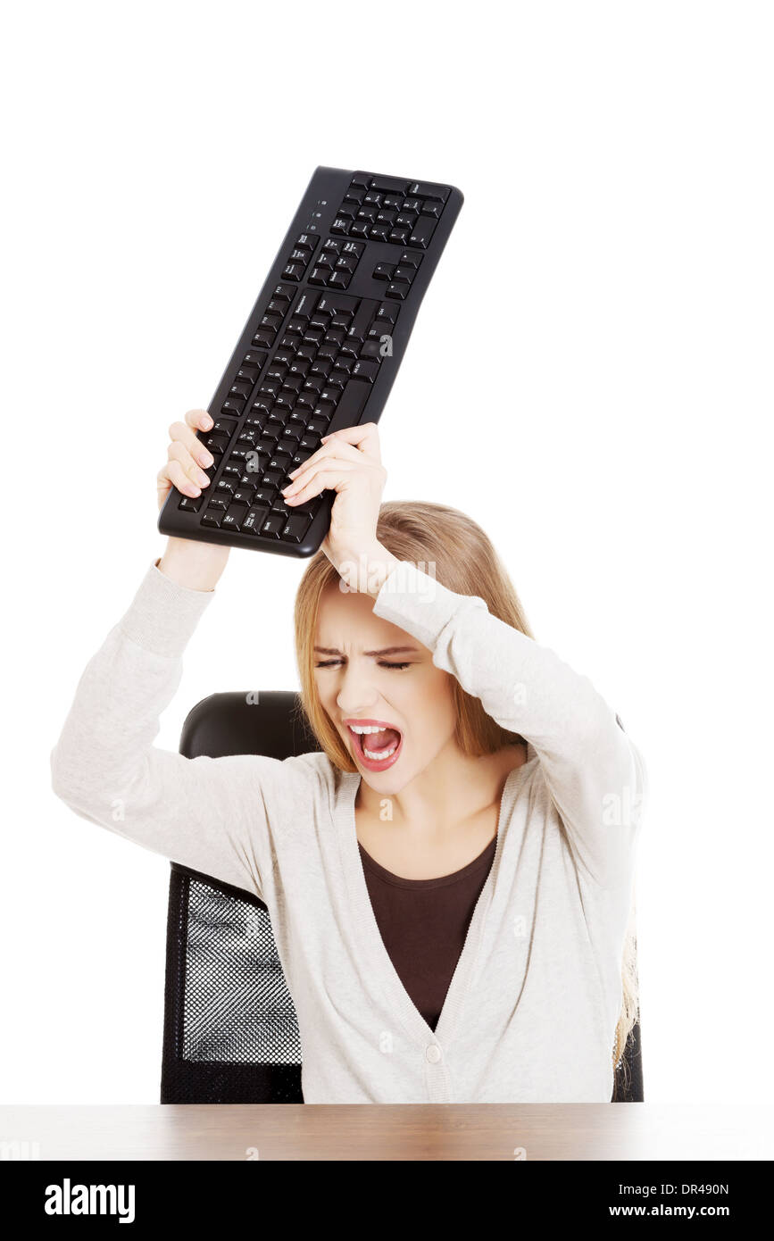 Beautiful casual woman behind the desk trying to broke the keyboard ...