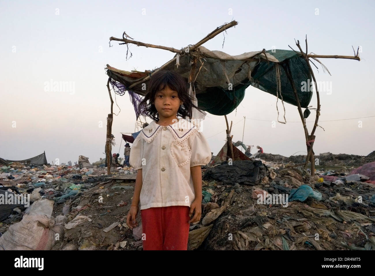 A young child laborer girl is standing near a ramshackle shelter at the ...
