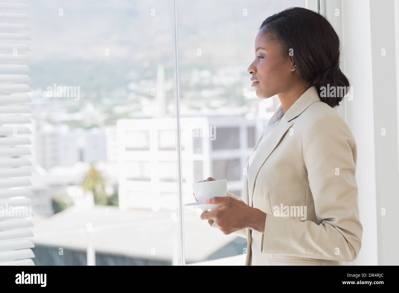 Elegant businesswoman with tea cup looking through office window Stock ...