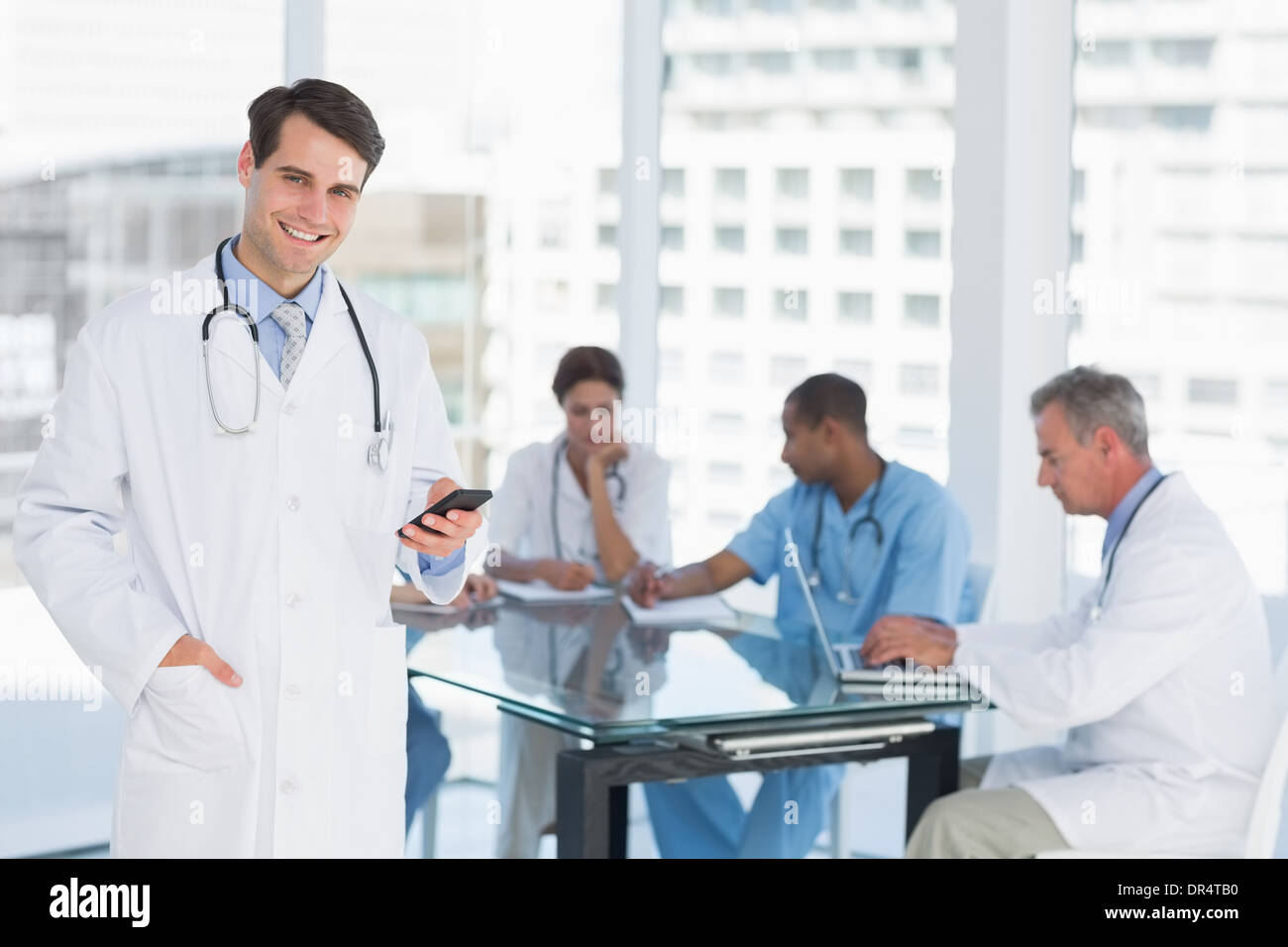 Doctor text messaging with group around table in background at hospital ...