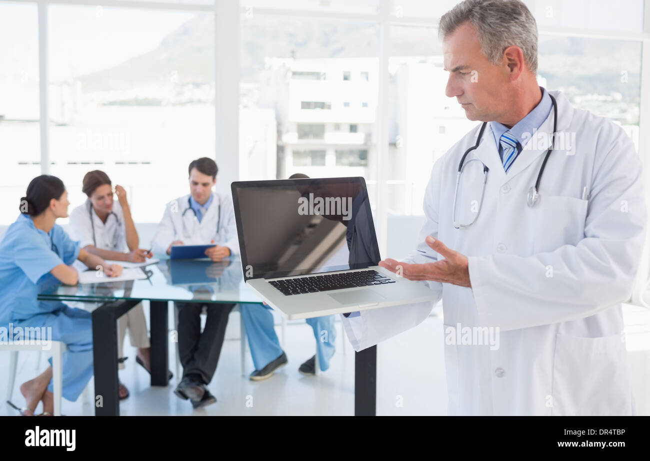 Doctor holding laptop with group around table in hospital Stock Photo ...