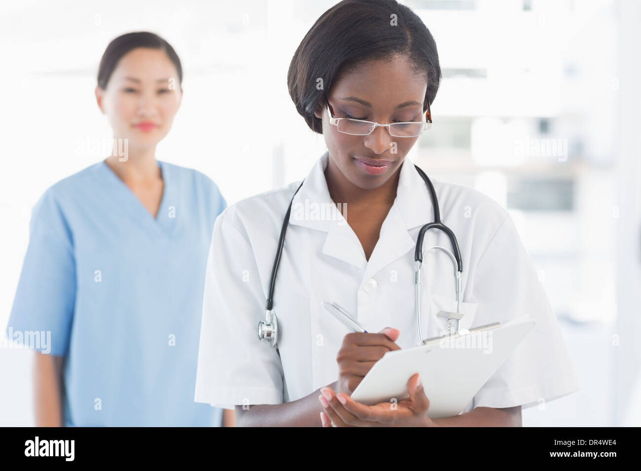 Female doctor writing report with surgeon in background Stock Photo - Alamy