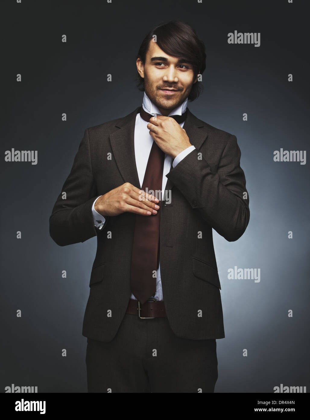 Portrait of good looking man in suit adjusting his necktie looking away ...