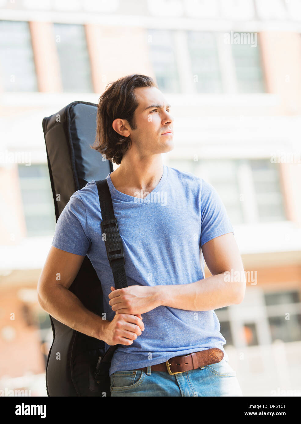 Caucasian man carrying guitar case on urban street Stock Photo - Alamy
