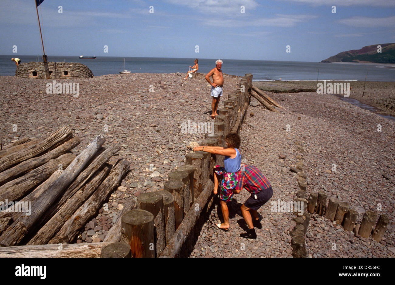 A partner struggles to lift a lady on a shingle beach up over a coastal ...