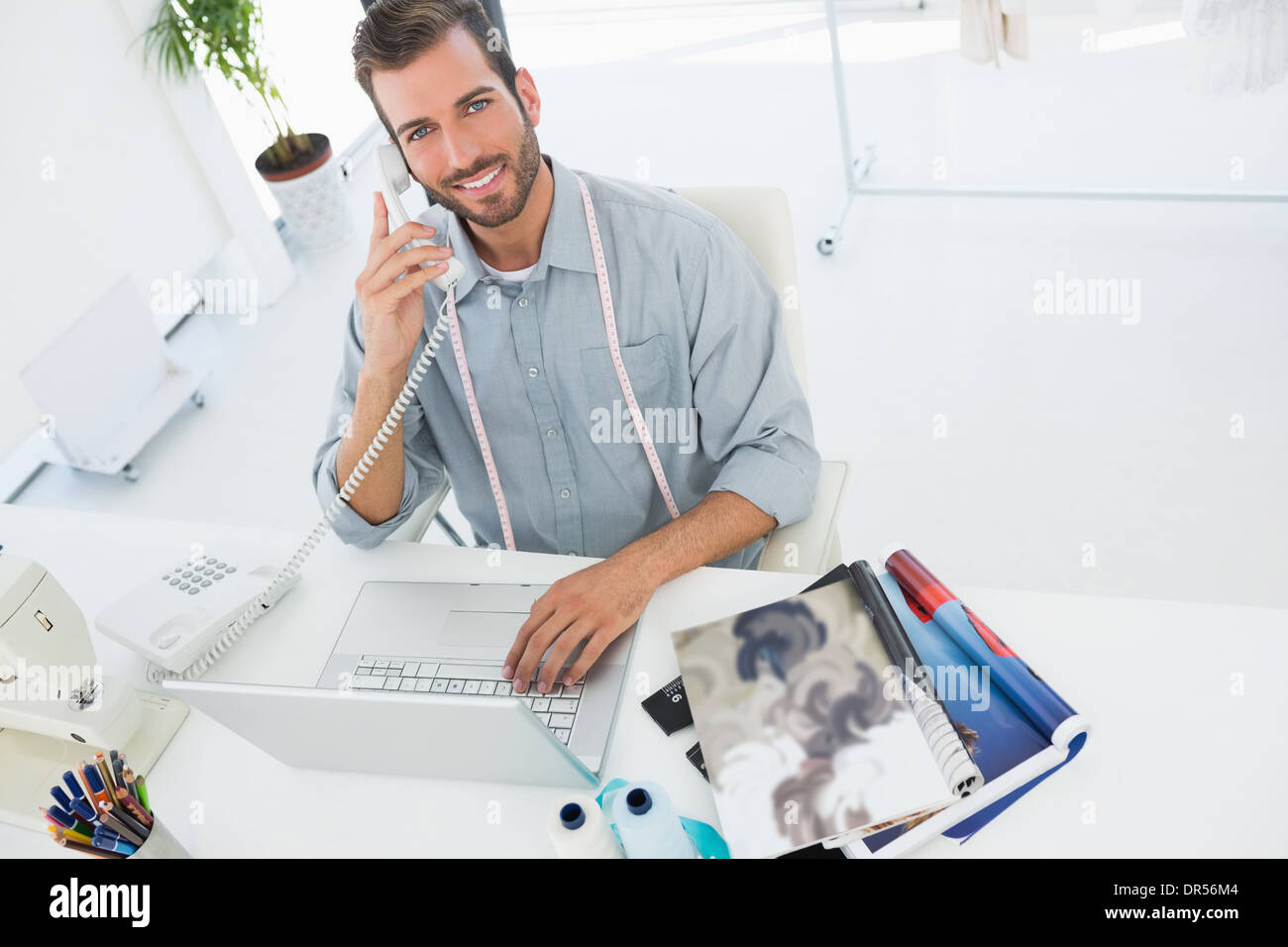 Fashion designer using laptop and phone in studio Stock Photo - Alamy