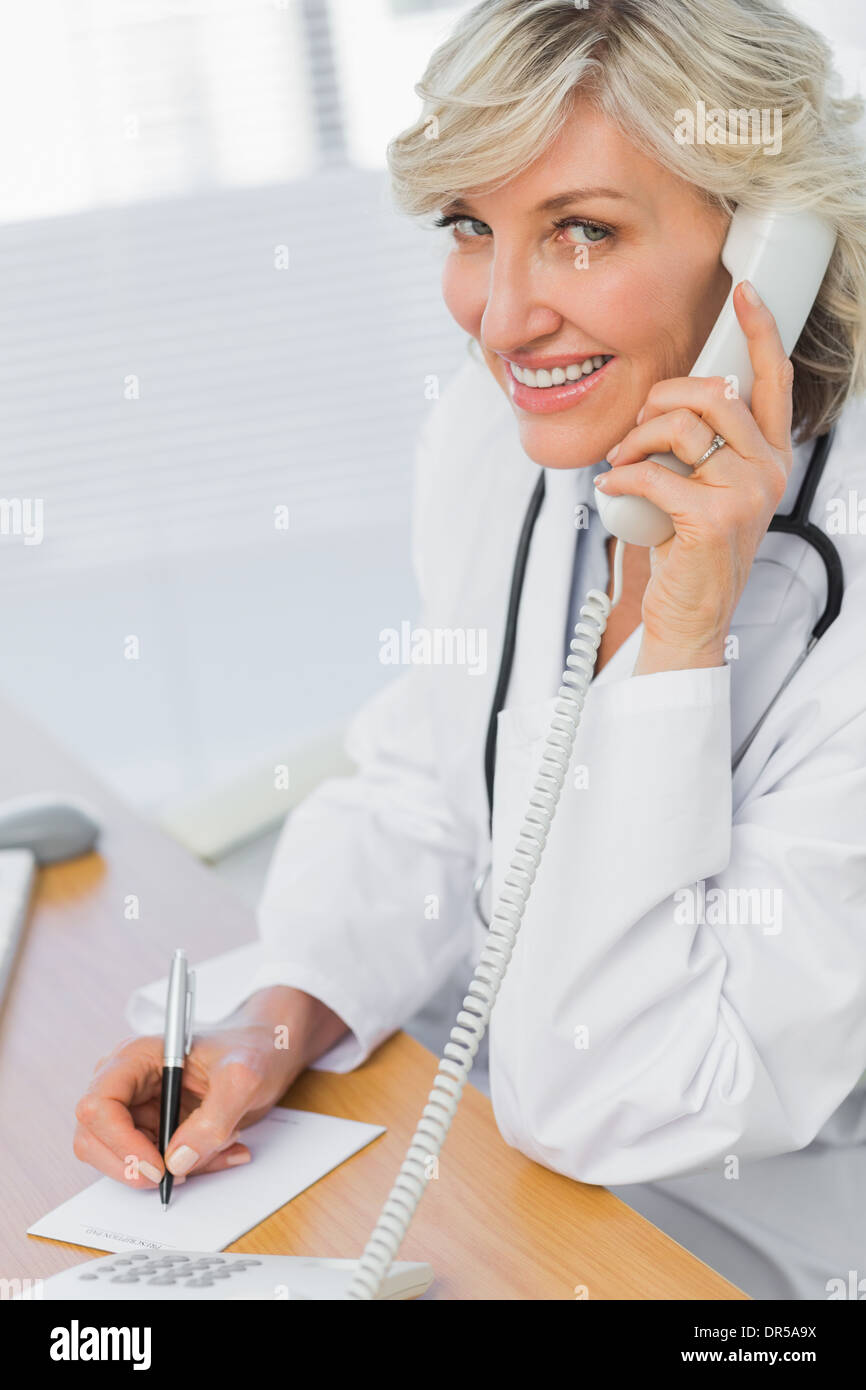 Female doctor using phone while writing notes Stock Photo - Alamy