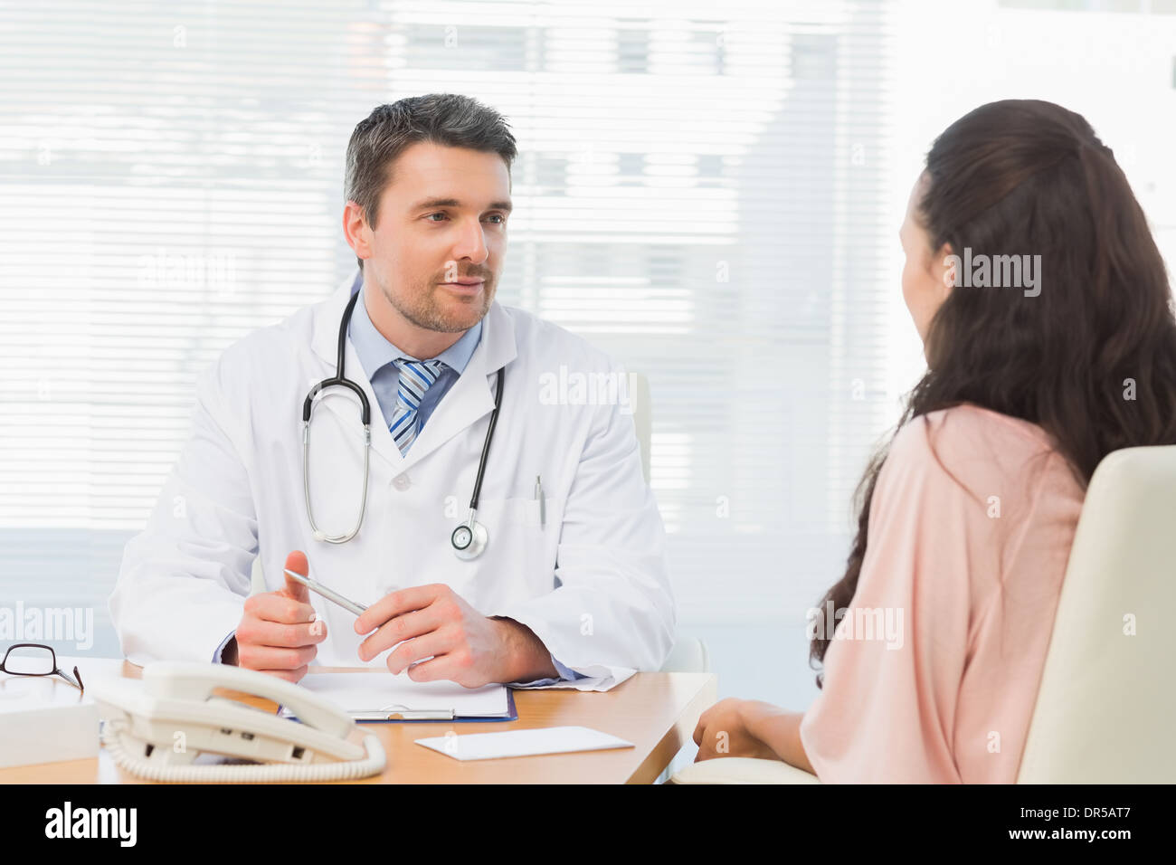 Doctor listening to patient with concentration at desk Stock Photo - Alamy