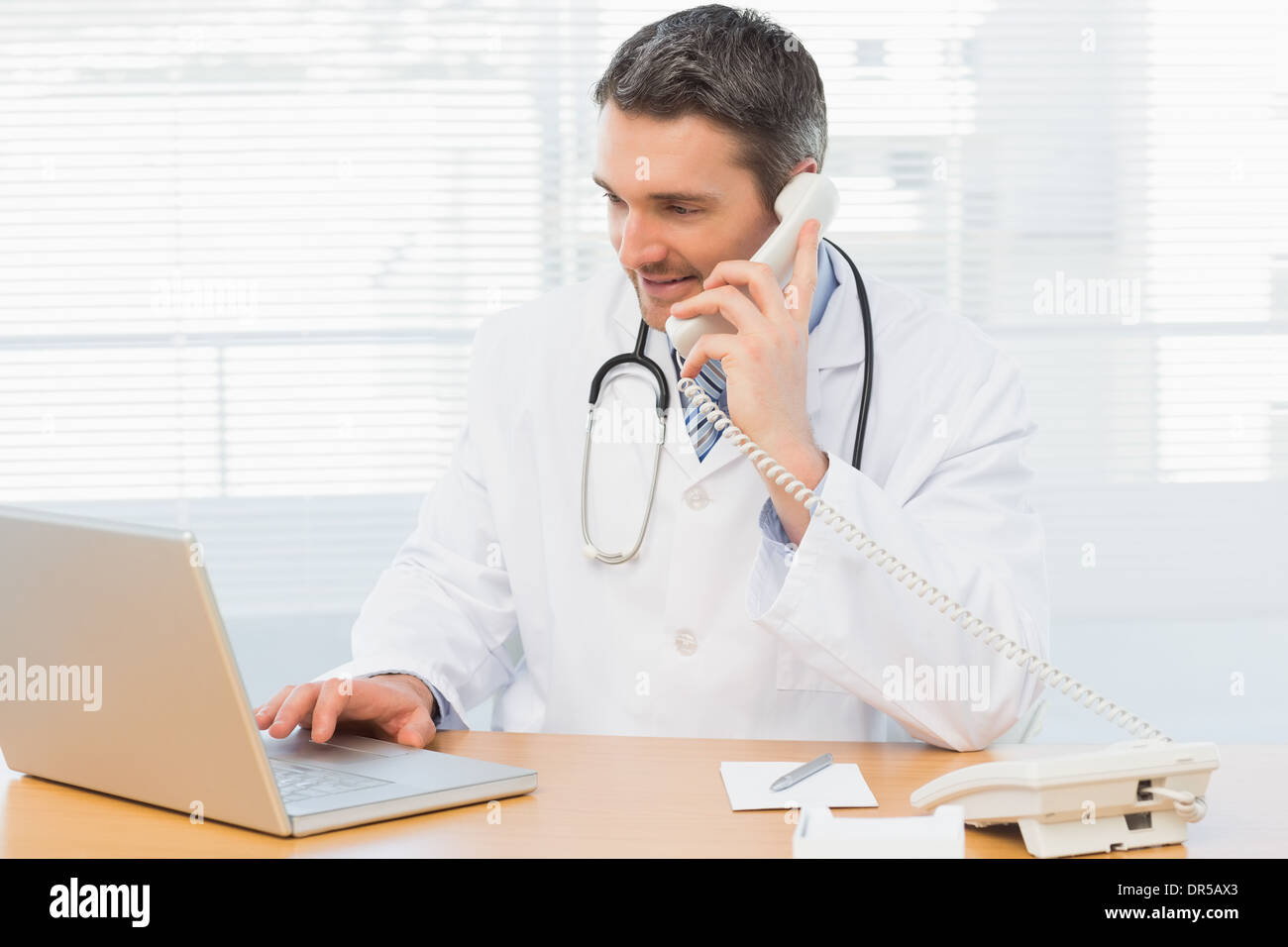 Concentrated doctor using laptop and phone Stock Photo - Alamy