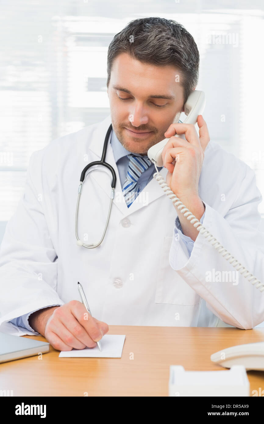 Concentrated doctor using phone while writing notes Stock Photo - Alamy