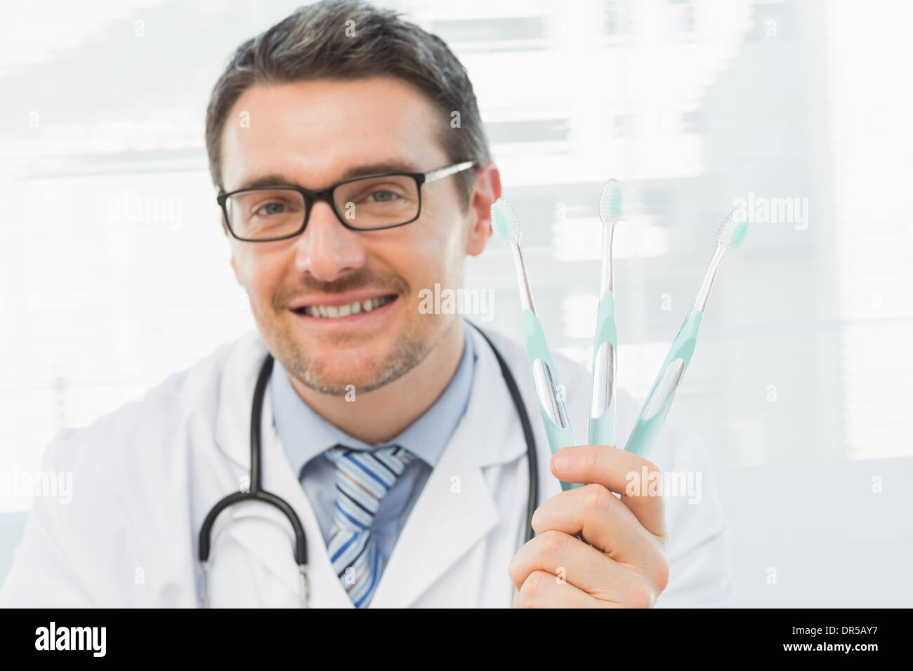 Smiling doctor holding toothbrushes in office Stock Photo - Alamy
