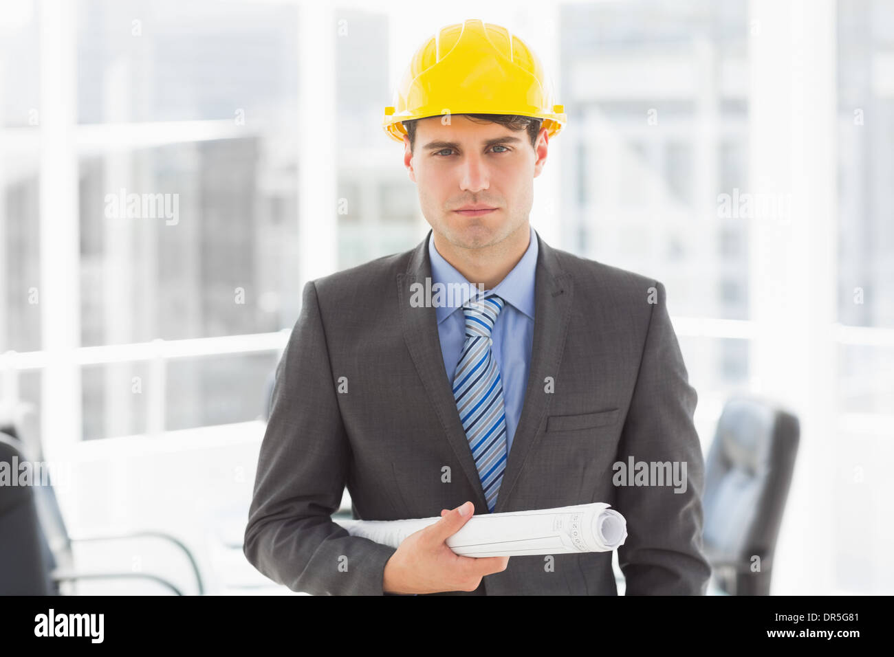 Serious architect holding blueprints looking at camera Stock Photo - Alamy