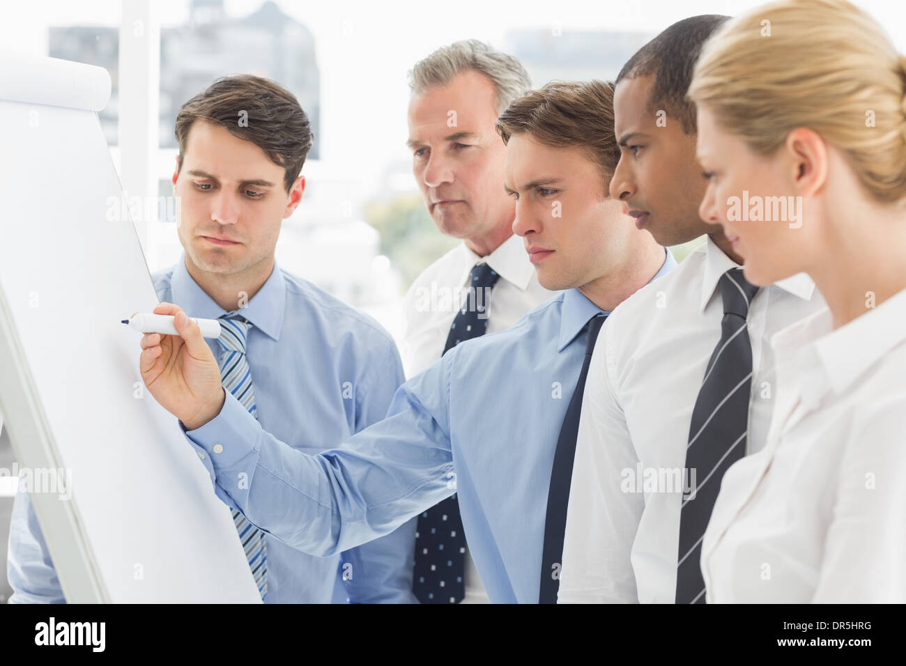 Colleagues watching young businessman write on whiteboard Stock Photo ...