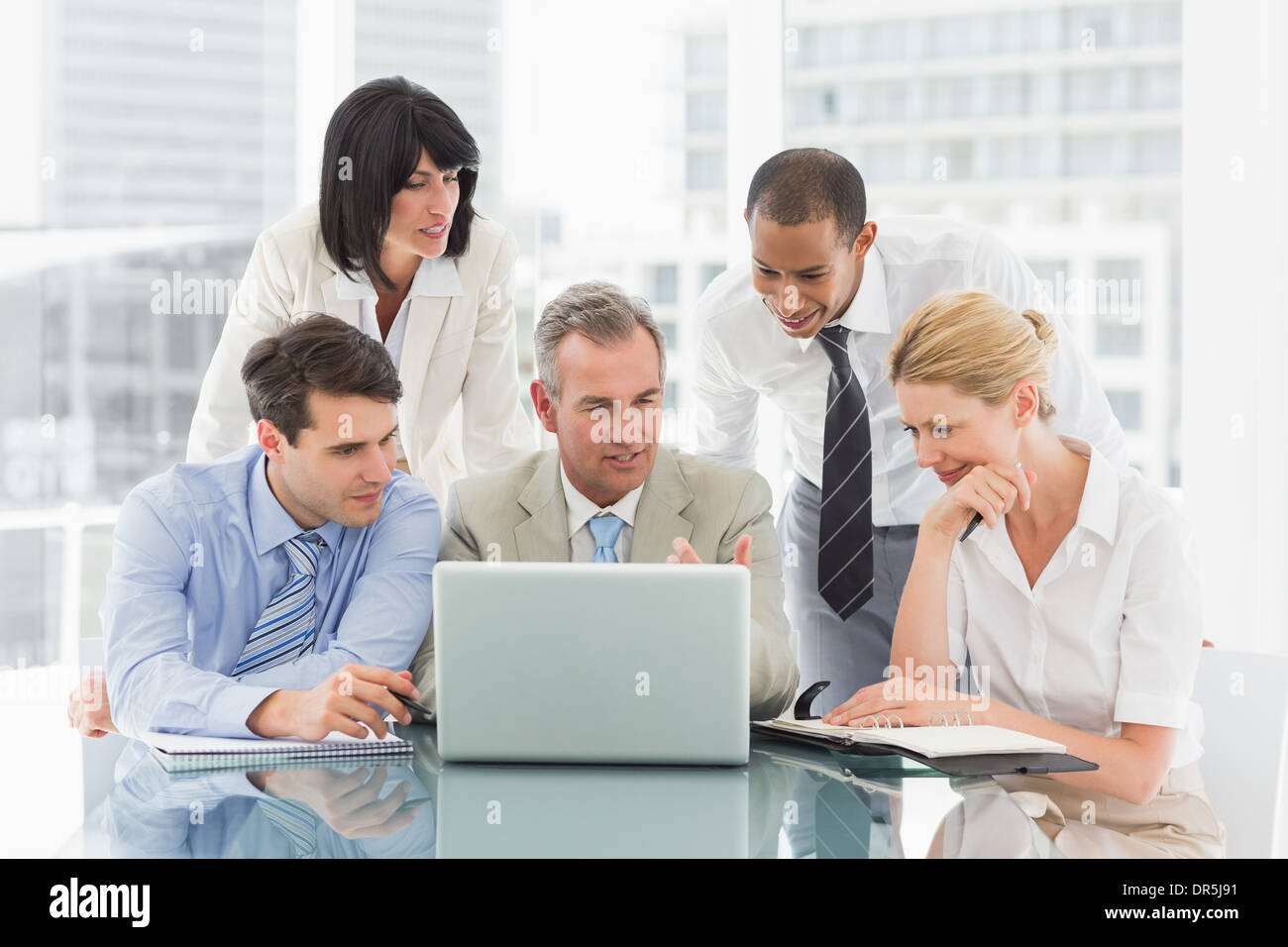 Happy business people gathered around laptop looking at it Stock Photo ...