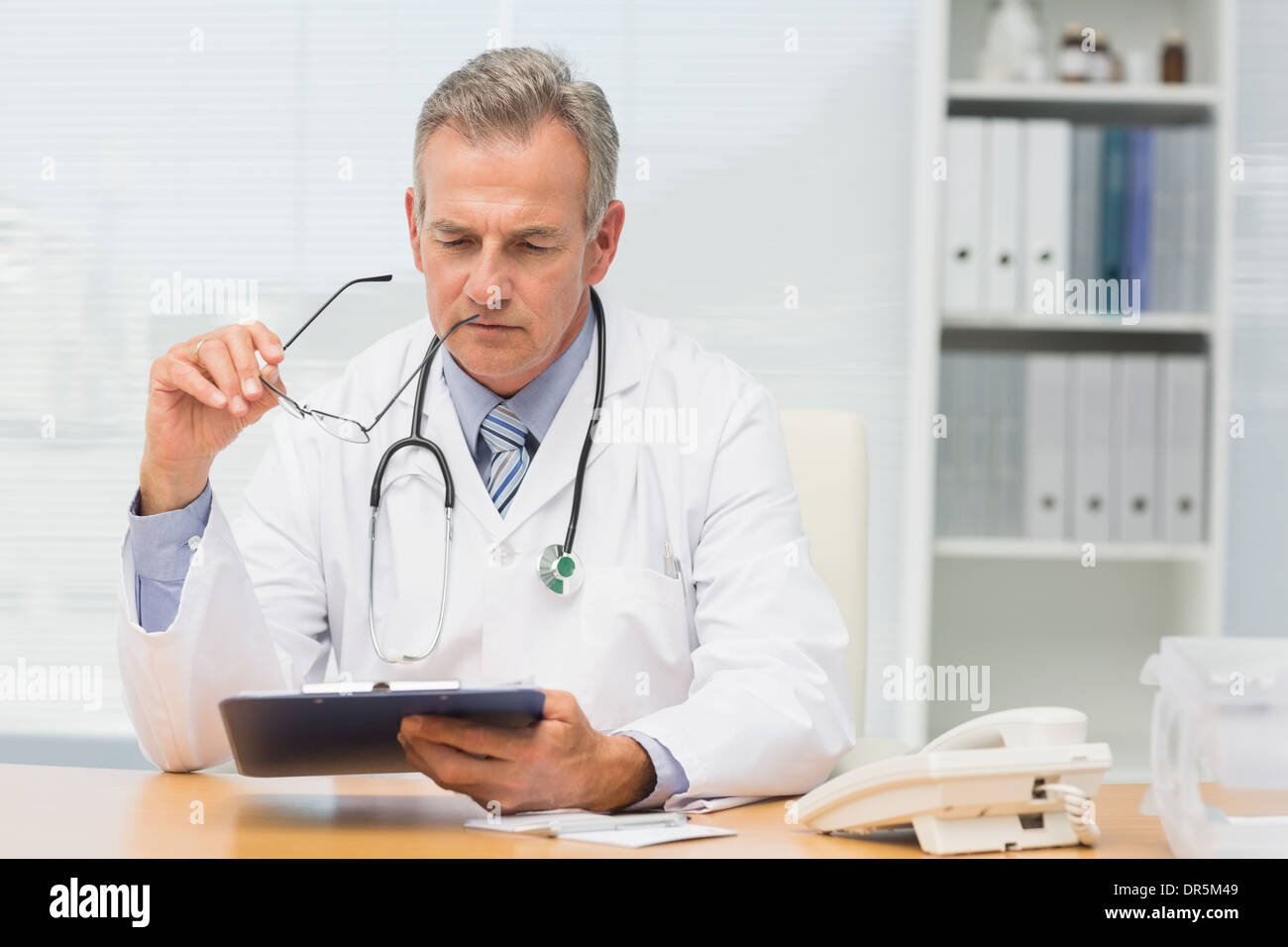 Focused doctor sitting at his desk with clipboard Stock Photo - Alamy