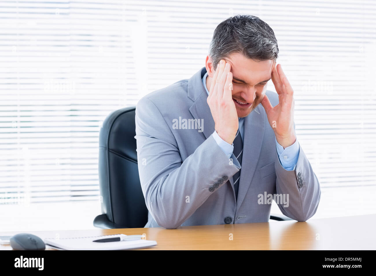 Businessman with severe headache at office desk Stock Photo - Alamy