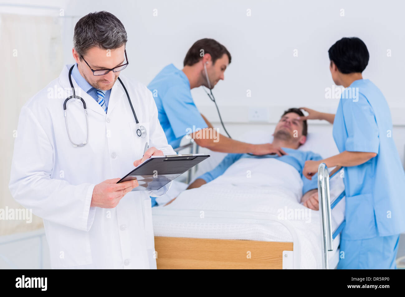 Doctor writing reports with patient and surgeons in background Stock ...