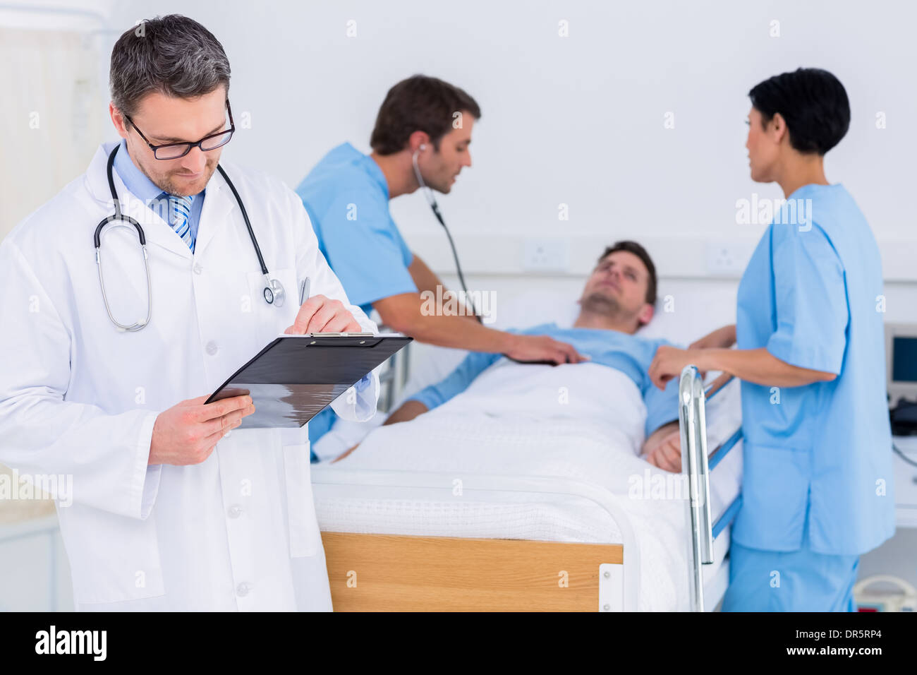 Doctor writing reports with patient and surgeons in background Stock ...