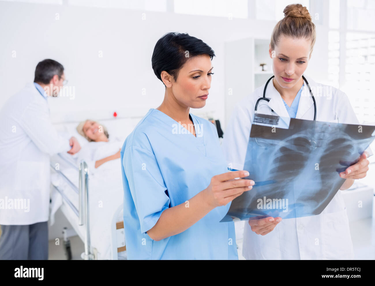 Doctors examining x-ray with patient in background Stock Photo - Alamy
