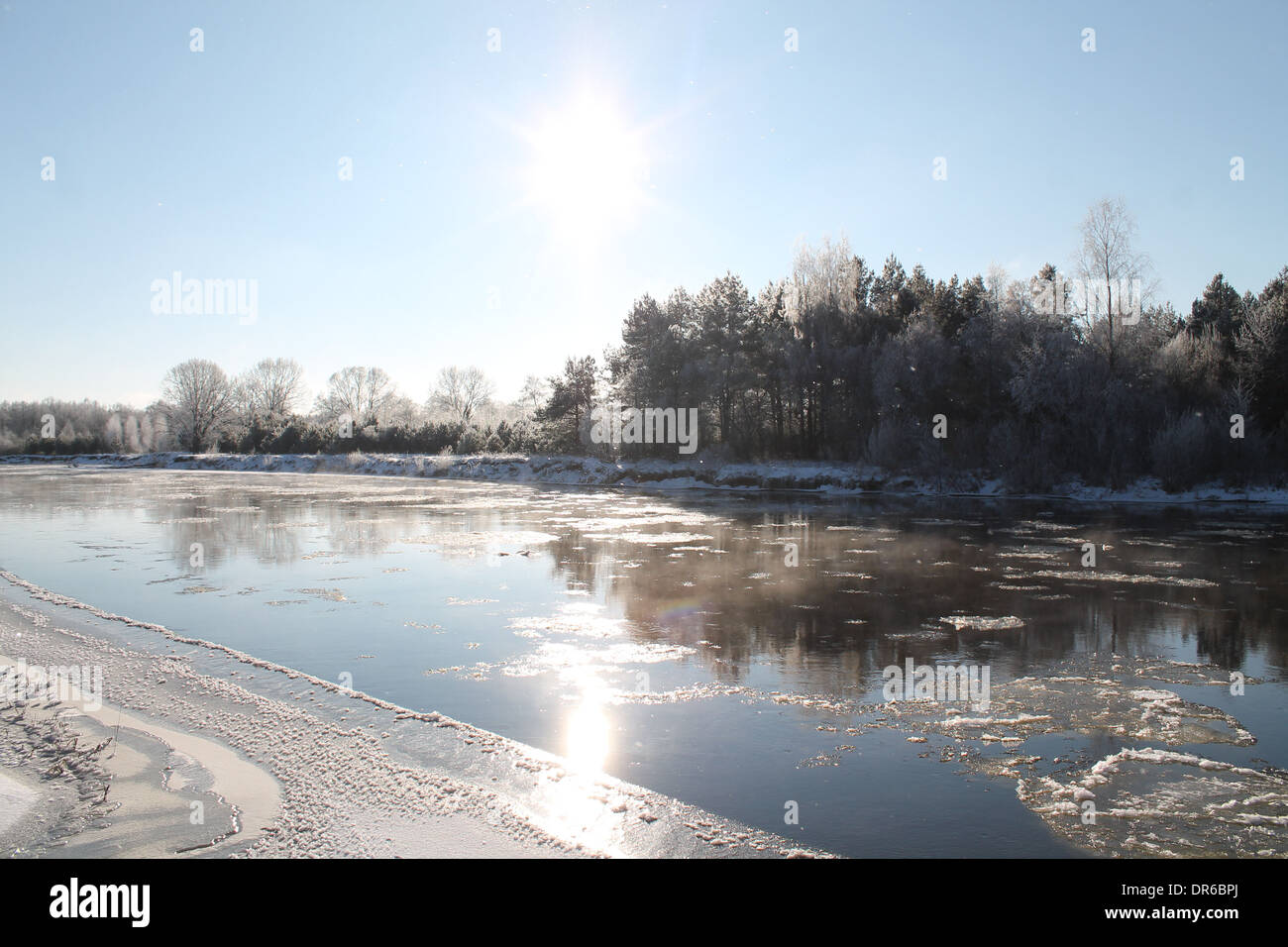 winter forest sinking in the snow on the bank on the calm frozen river ...