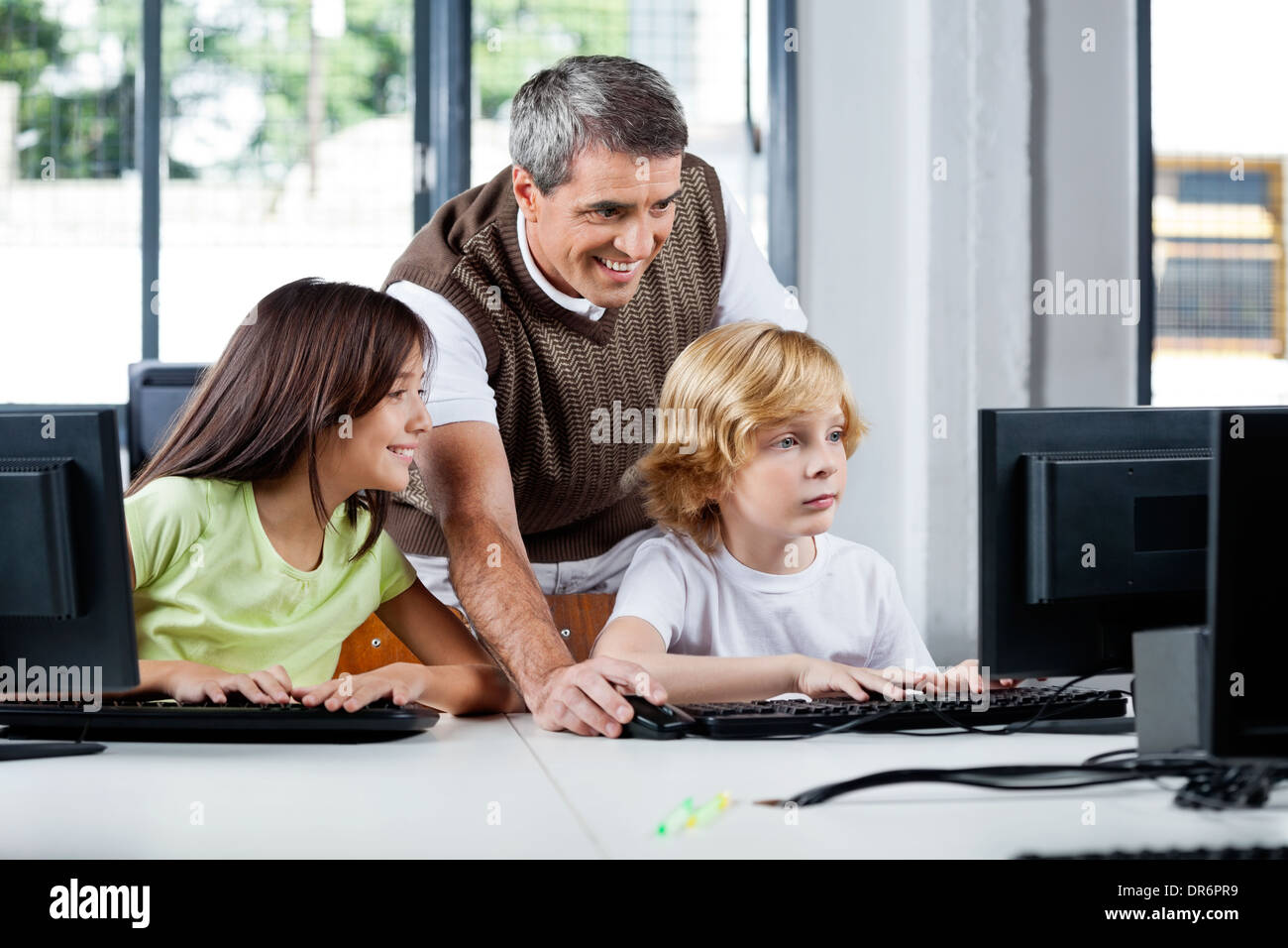Happy Teacher Assisting Schoolchildren In Using Desktop Pc Stock Photo ...