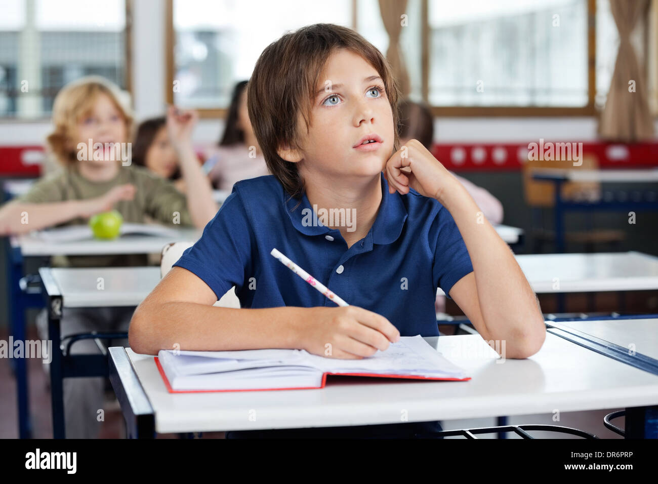 Boy Looking Up While Writing At Desk Stock Photo - Alamy