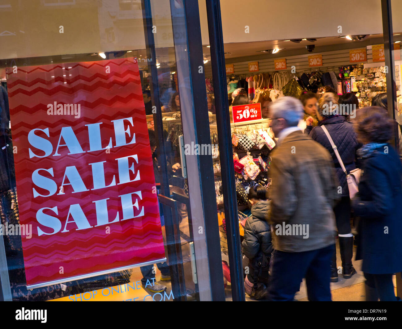Busy high street shop at dusk with sale banner in window and customers ...