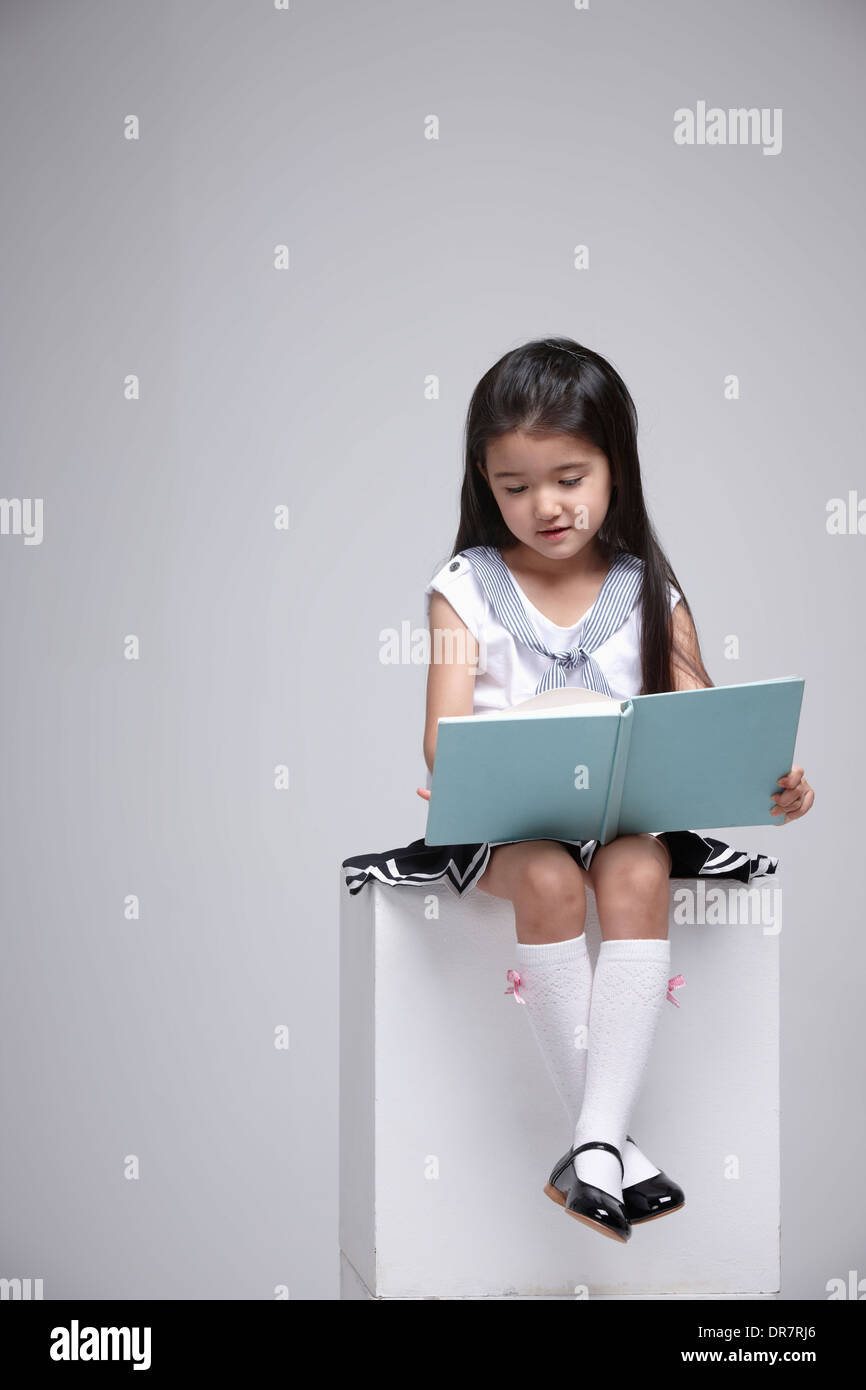 a girl sitting on a box reading a book Stock Photo - Alamy