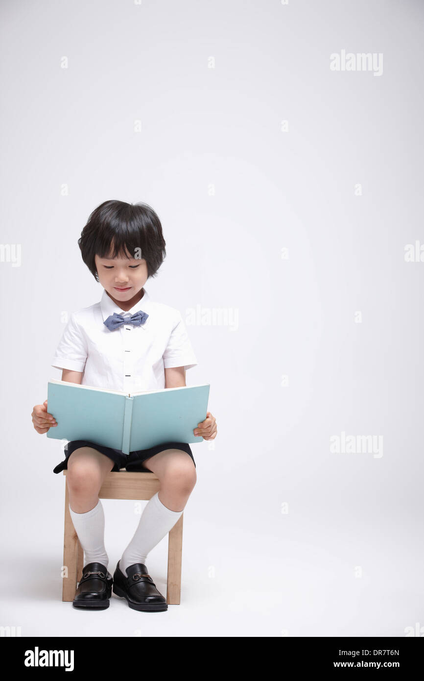 a boy sitting on a chair reading a book Stock Photo - Alamy