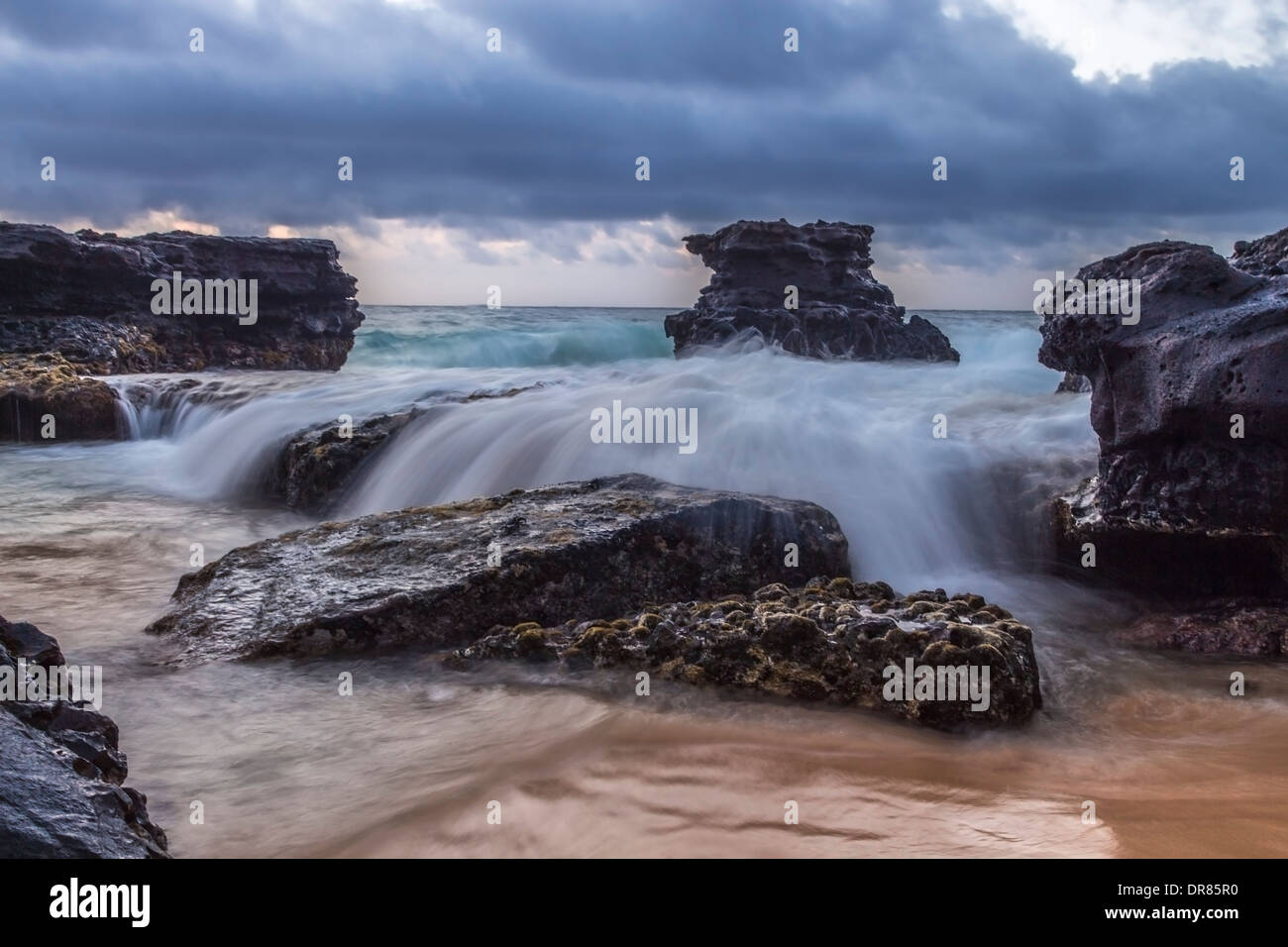 The ocean cascading over exposed rock outcropping at sunrise at Sandy ...
