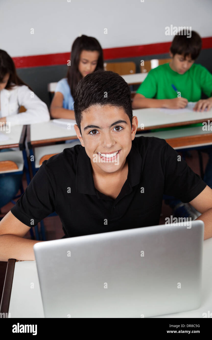 Happy Teenage Schoolboy Sitting With Laptop In Classroom Stock Photo ...