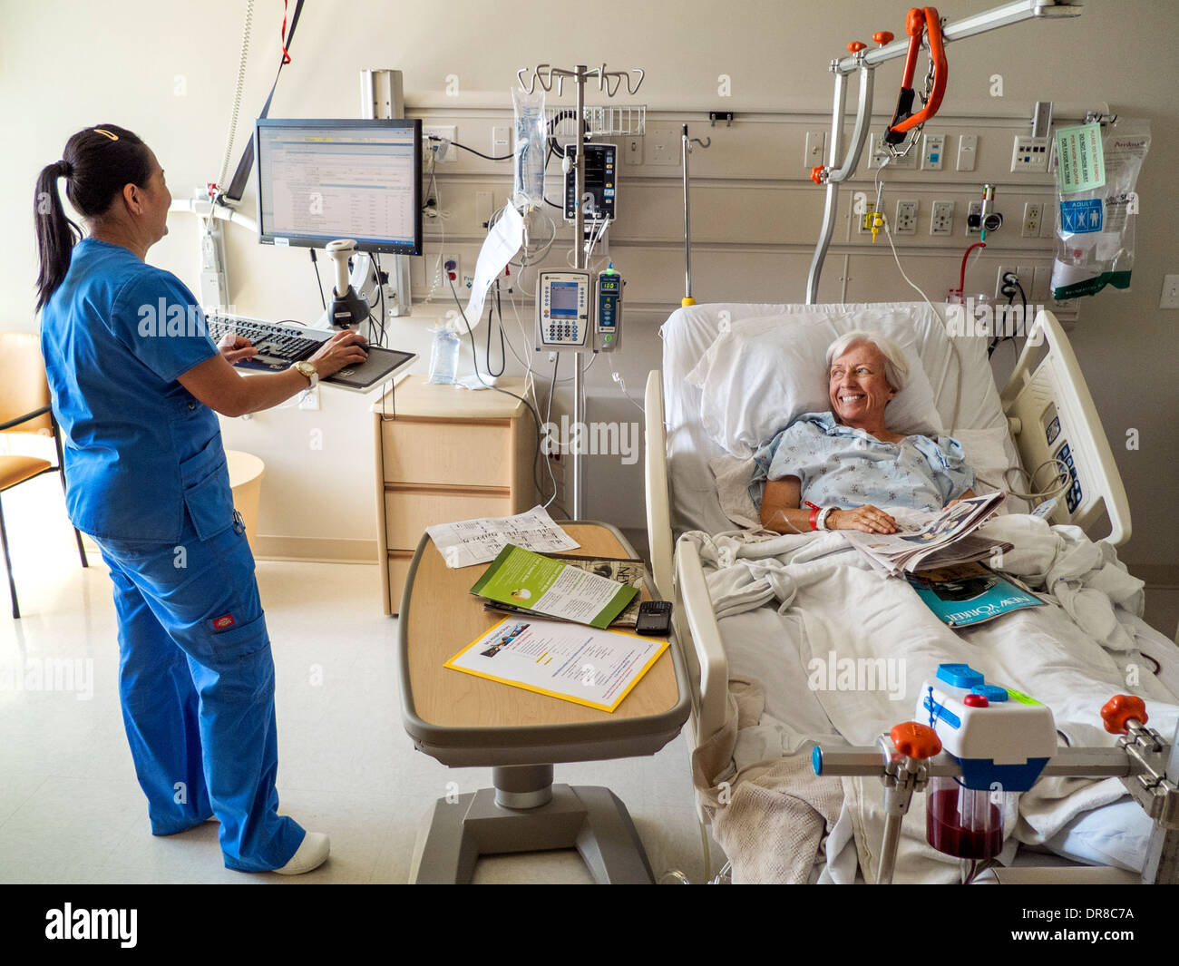 Recovering surgery patient jokes with a nurse reading her medical data ...