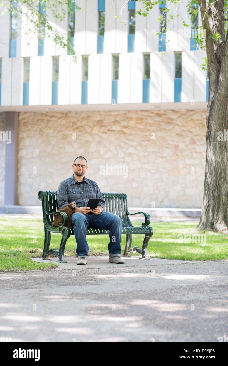 Mid Adult Student Sitting On Bench At Campus Stock Photo - Alamy