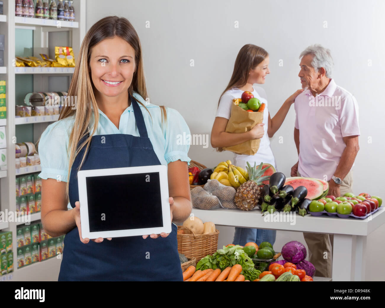 Saleswoman Displaying Tablet With Customers In Background Stock Photo ...