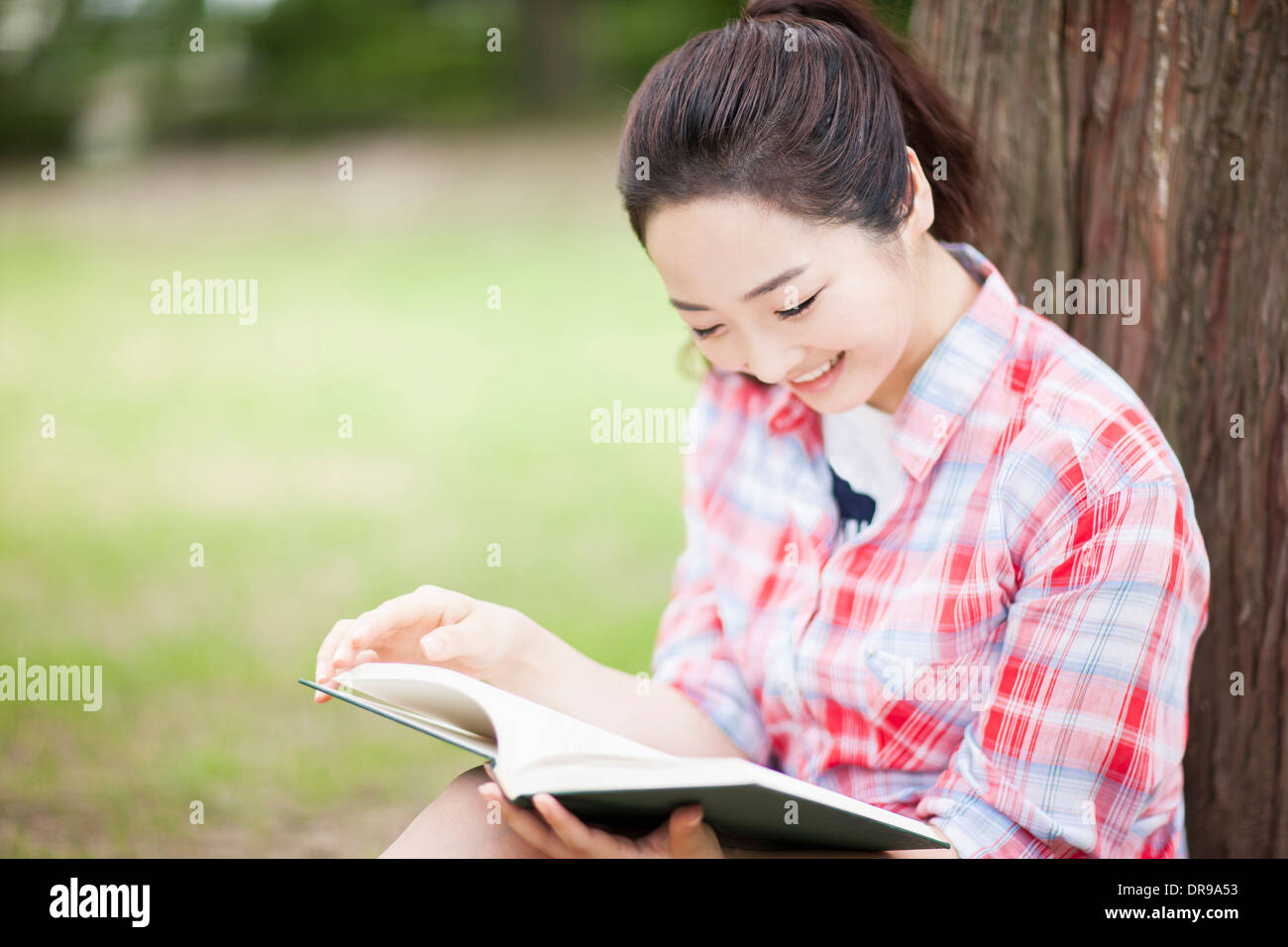 a woman leaning on tree reading a book Stock Photo - Alamy