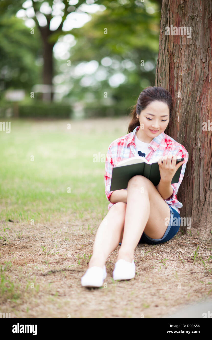 a woman leaning on tree reading a book Stock Photo - Alamy