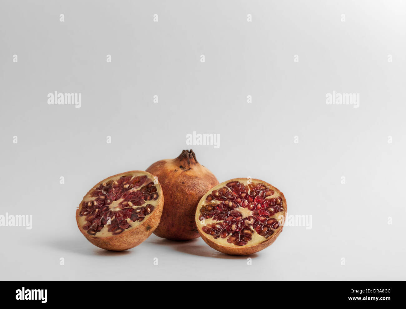 Two edible pomegranates on a white background with one cut open showing ...