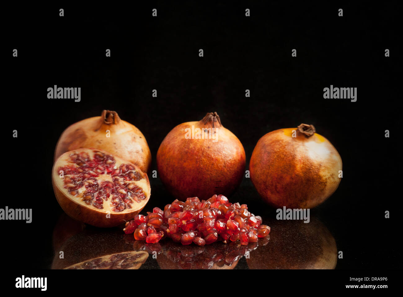 3 pomegranates in a row with a half pomegranate open and with the seeds ...